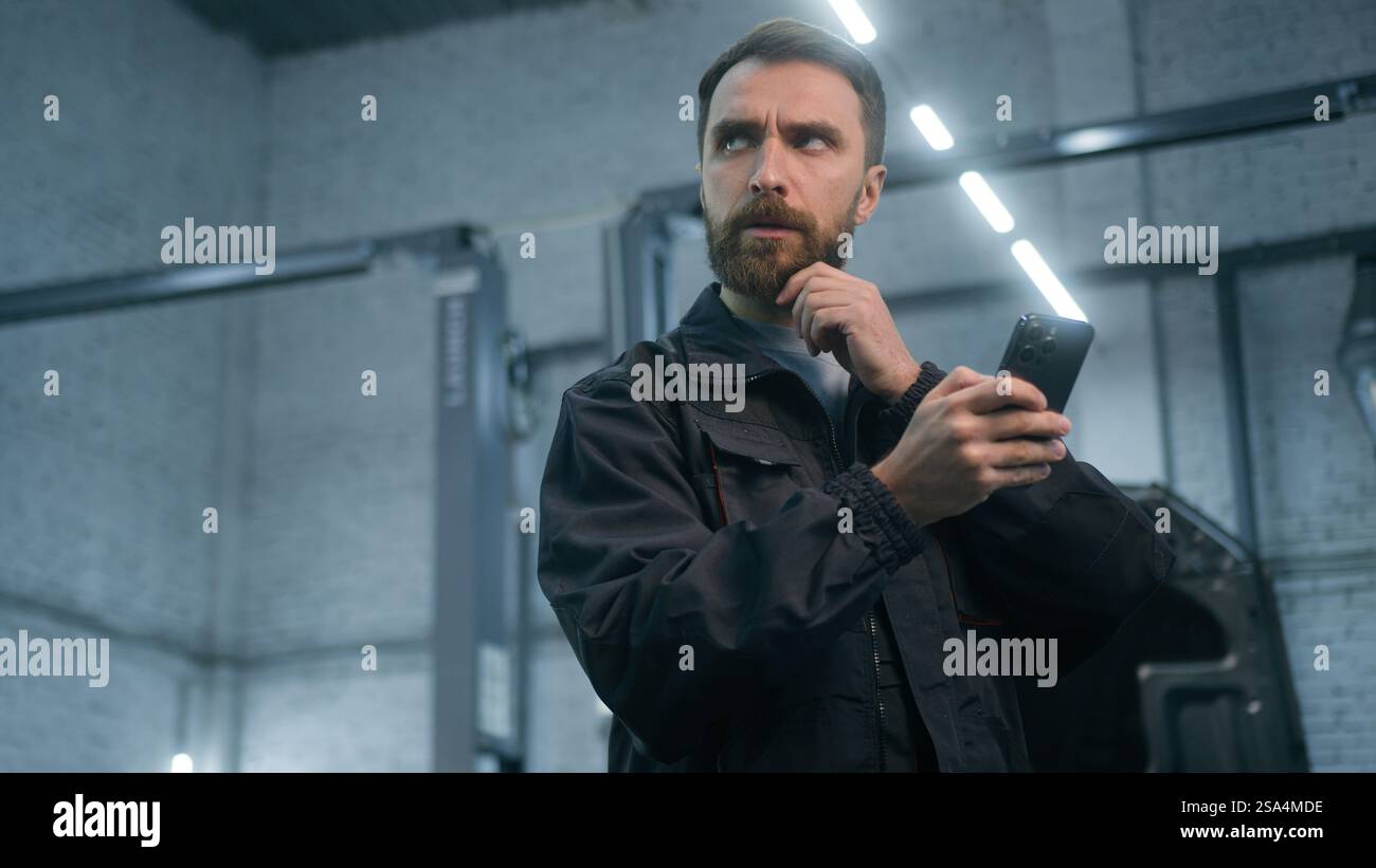 Thoughtful male mechanic using mobile hi-res stock photography and ...