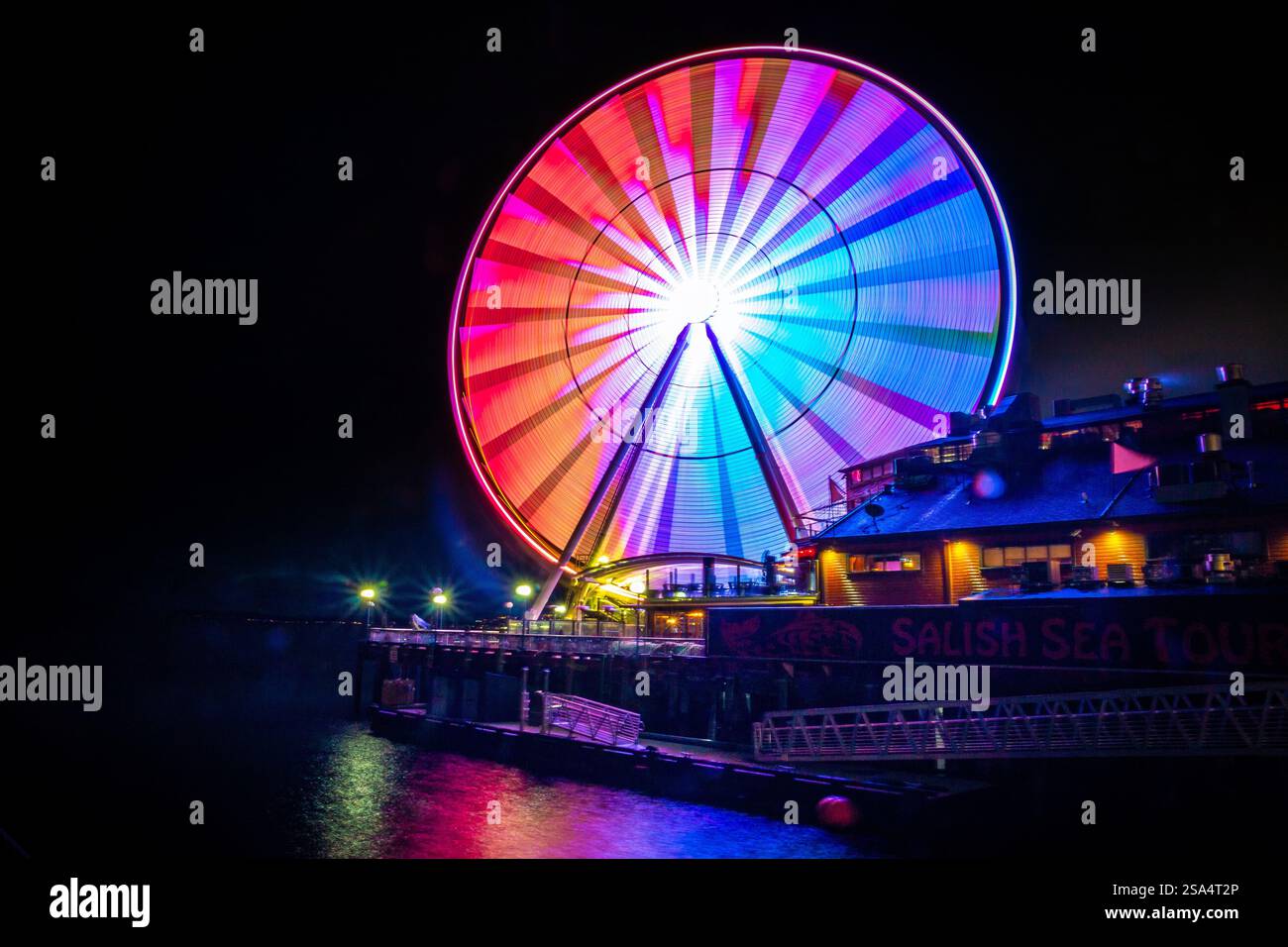 The Seattle Great Wheel glows brightly at night, with colorful ...