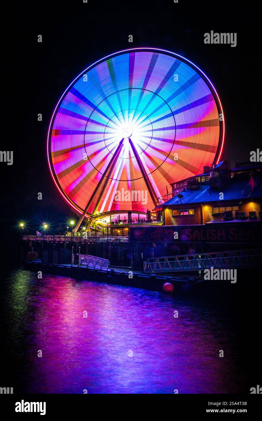 The Seattle Great Wheel glows brightly at night, with colorful ...