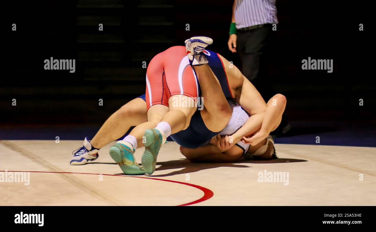 Two wrestlers grapple on the mat during a competitive event at a high school gym under a spot ...