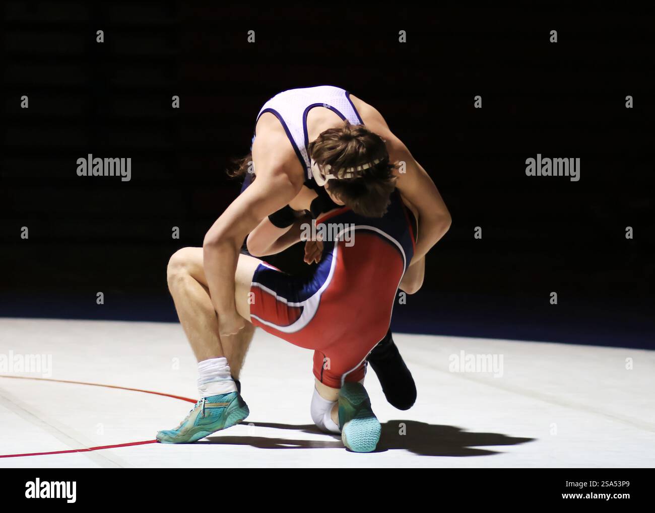 Two athletes grapple intensely on the wrestling mat under bright lights ...