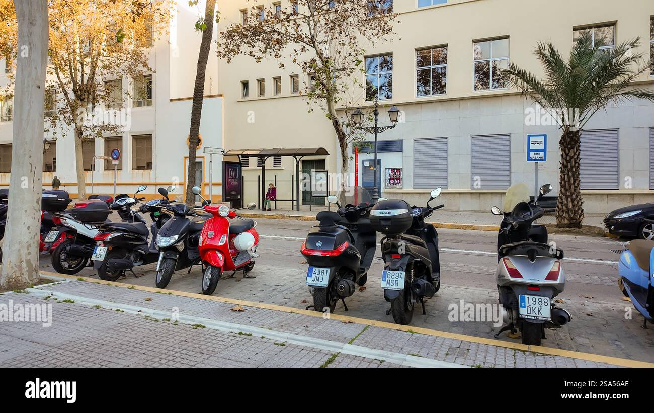 Scooters parked on the side of a road in Cádiz, Spain, lined up against ...