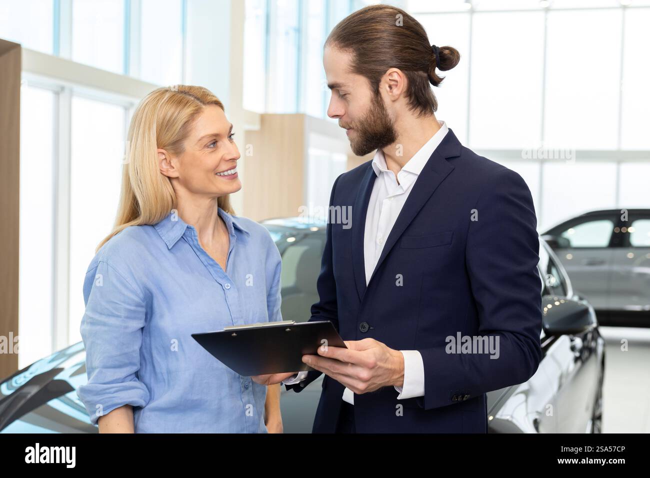 Male dealership representative showing new car models to a female ...