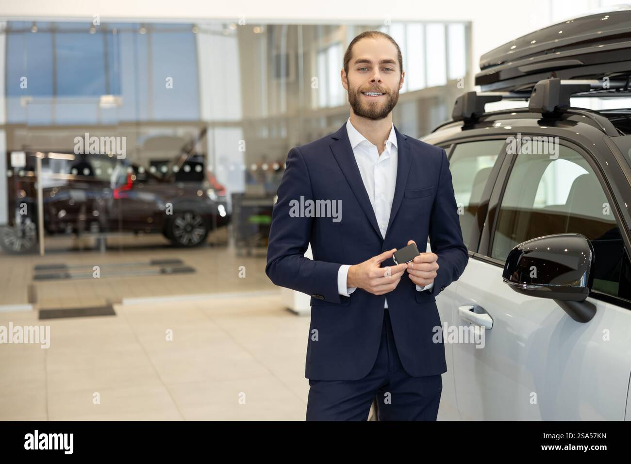 Elegant man standing near the cars in a dealership and holding car key ...
