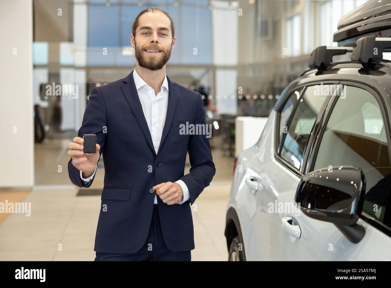 Elegant man standing near the cars in a dealership and holding car key ...