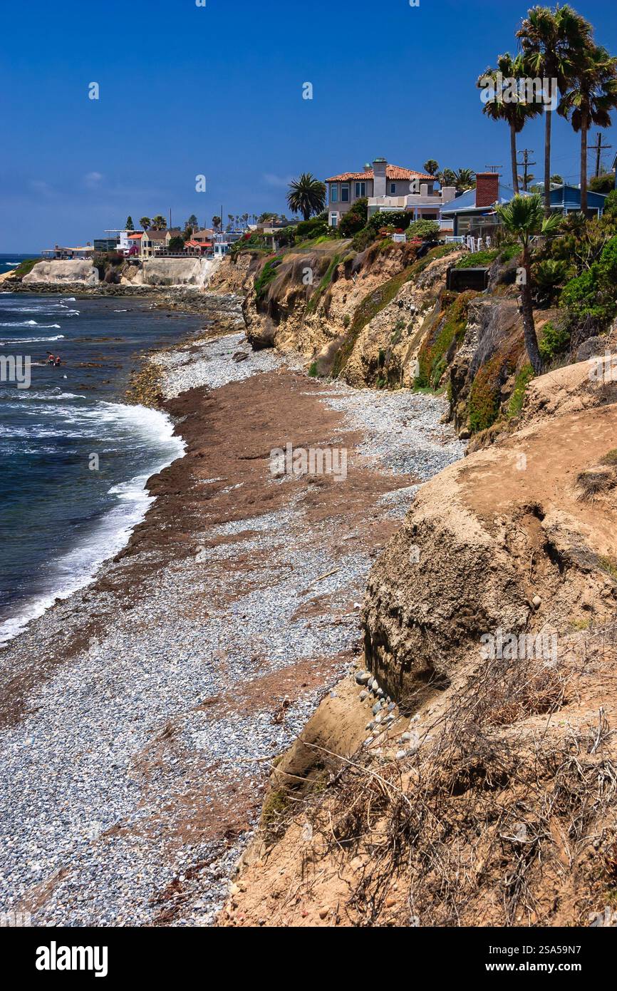 A beach with a rocky cliff and a house in the distance. The beach is ...