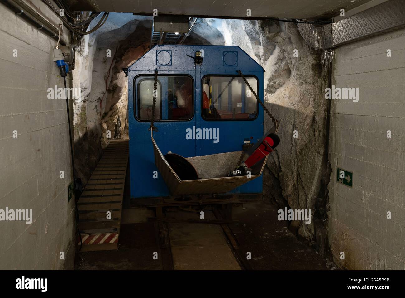 A blue mining cart awaits in a rocky tunnel, illuminated by soft ...