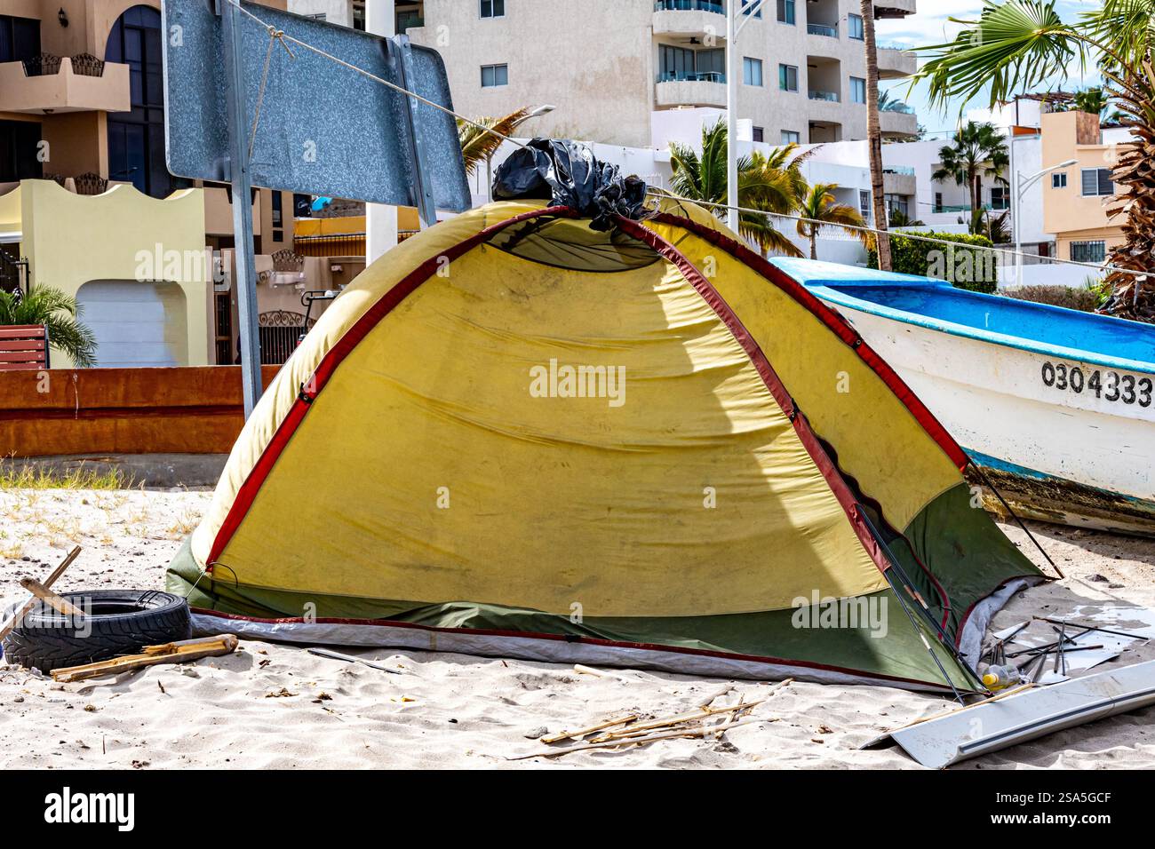 Old and worn yellow tent on beach sand next to rowboat, temporary ...