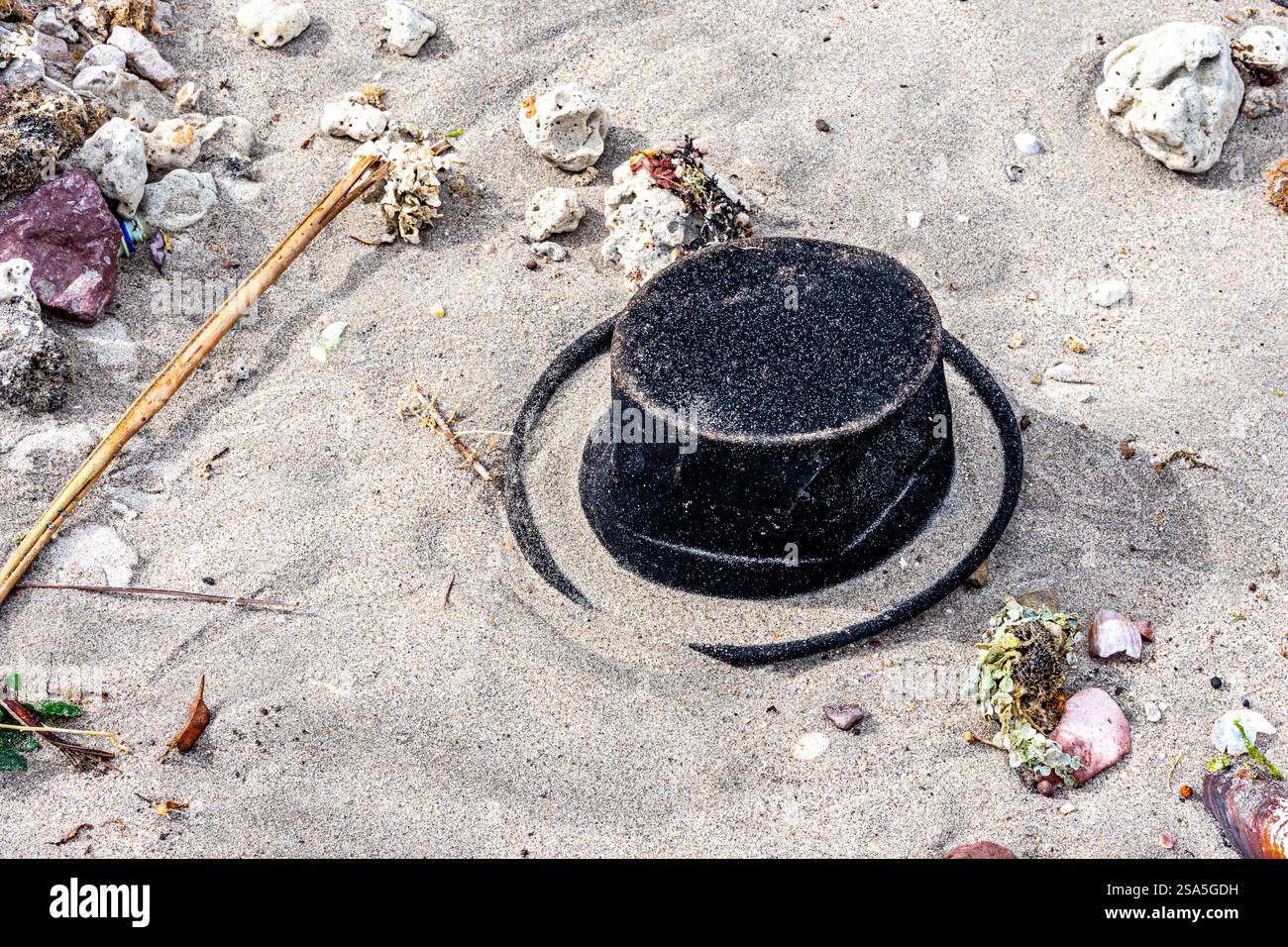 Black top hat lying on sand of beach partially covered with sand ...