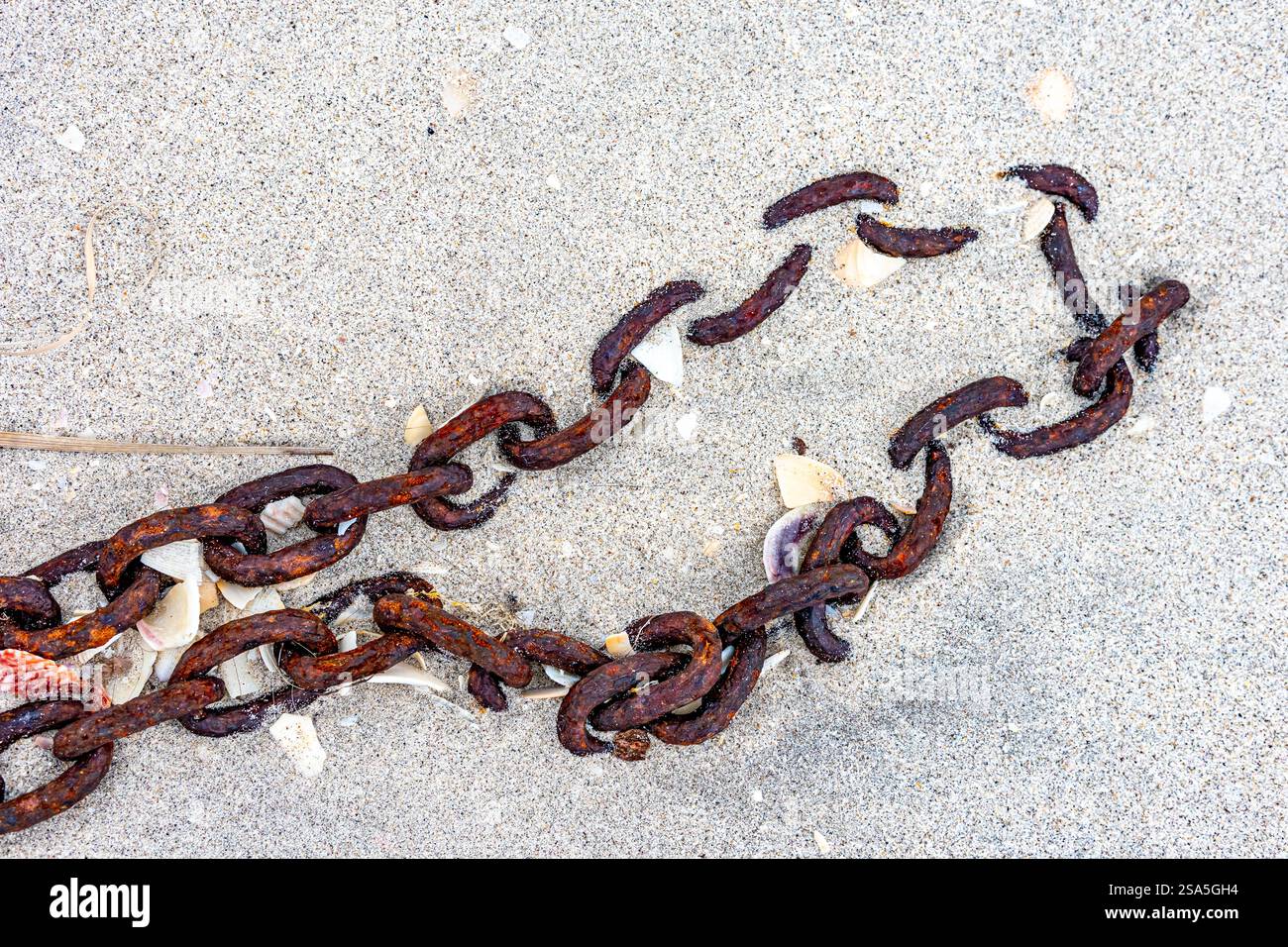 Beach shore with rusty metal chain lying on sand, remains of broken ...