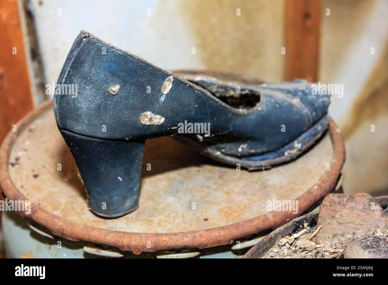 A dirty old shoe sits on a rusty metal barrel. The shoe is worn and has ...