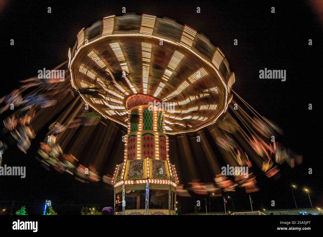 A carnival ride is spinning in the dark. The lights on the ride are ...