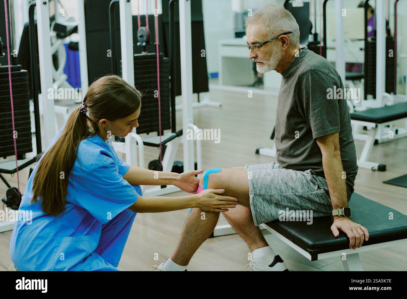 High angle shot of young rehab coach taping knee of elderly patient who ...