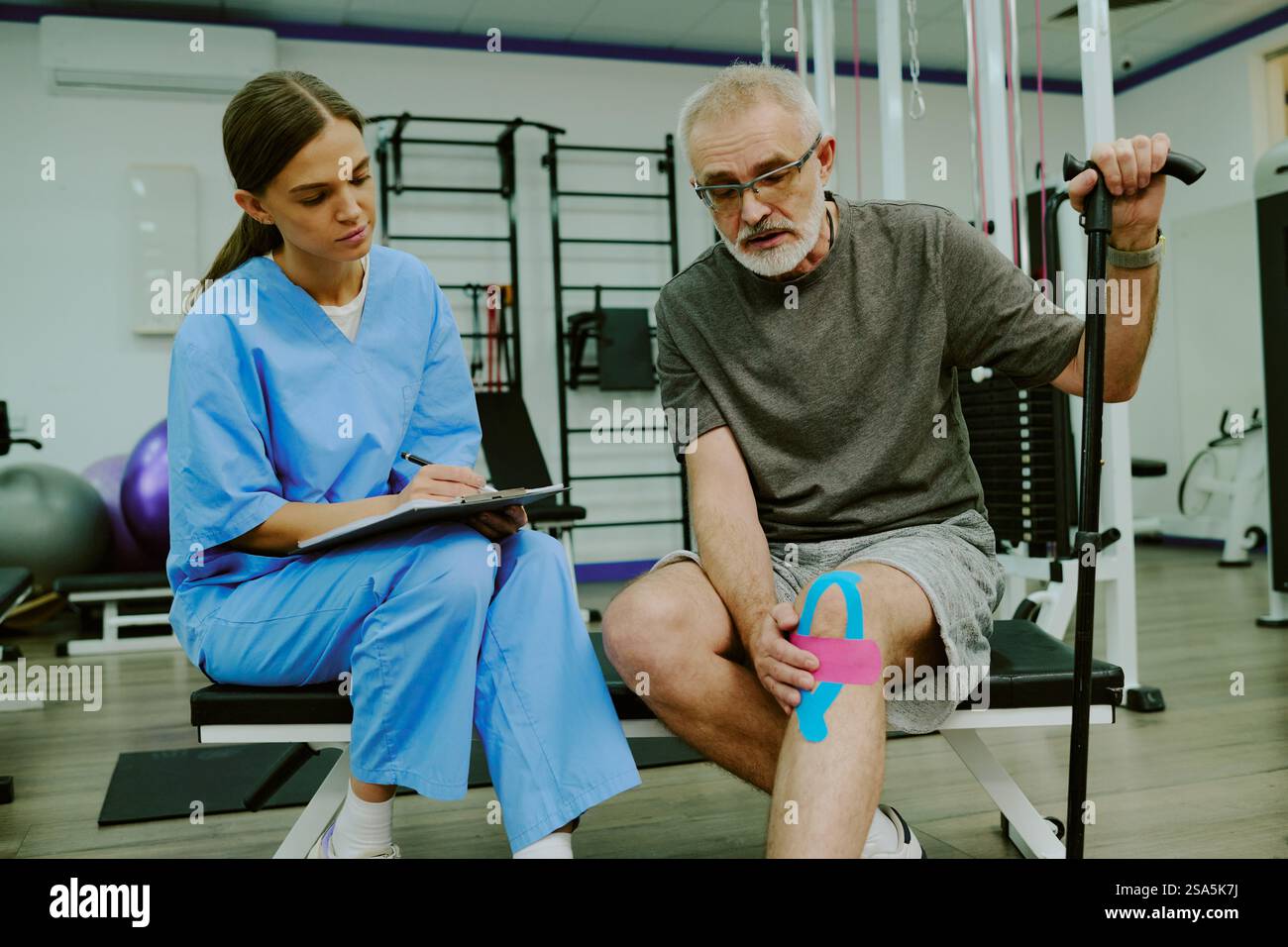 Medium close up of elderly man with cane in hand touching taped knee ...