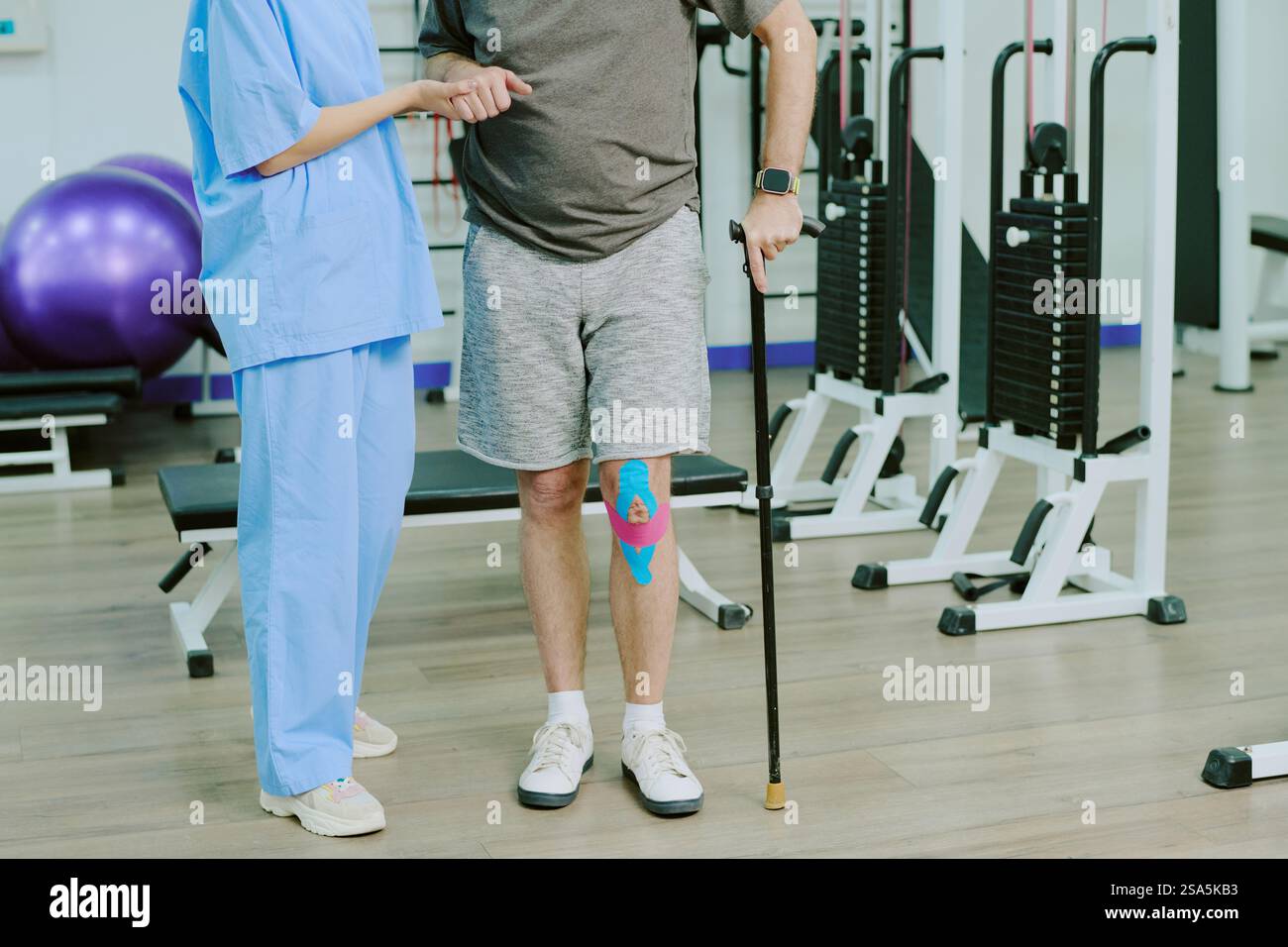 Unrecognizable rehab trainer supporting elderly man during walk while ...