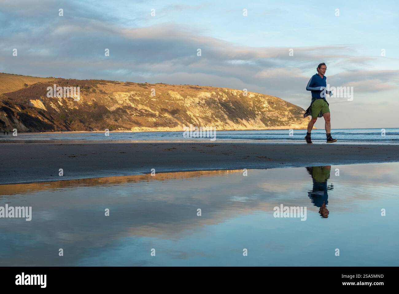 Jogger enjoying sunset stroll along Swanage Beach with Ballard Cliff in ...