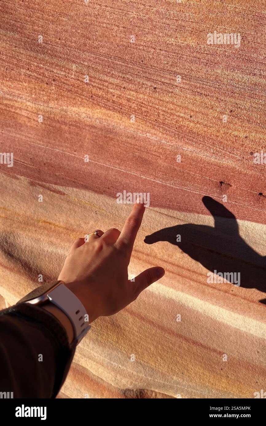 A hand points towards the natural patterns of colorful rock layers ...