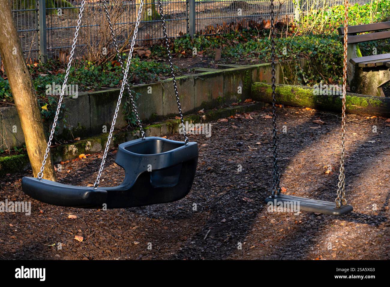 Two swings hang in a peaceful playground, one designed for infants and ...