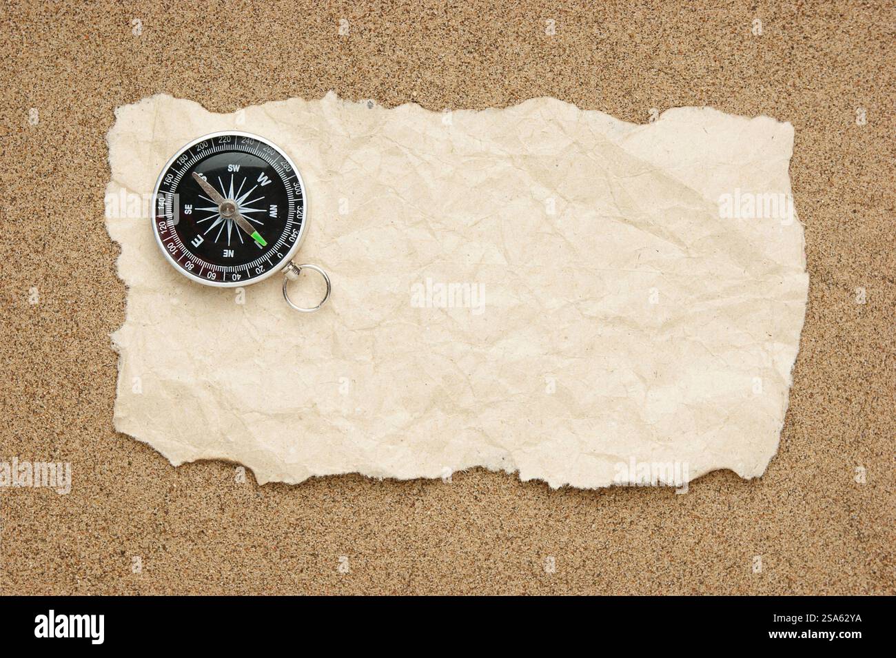 Compass on old sheet crumpled paper against the background of sand ...