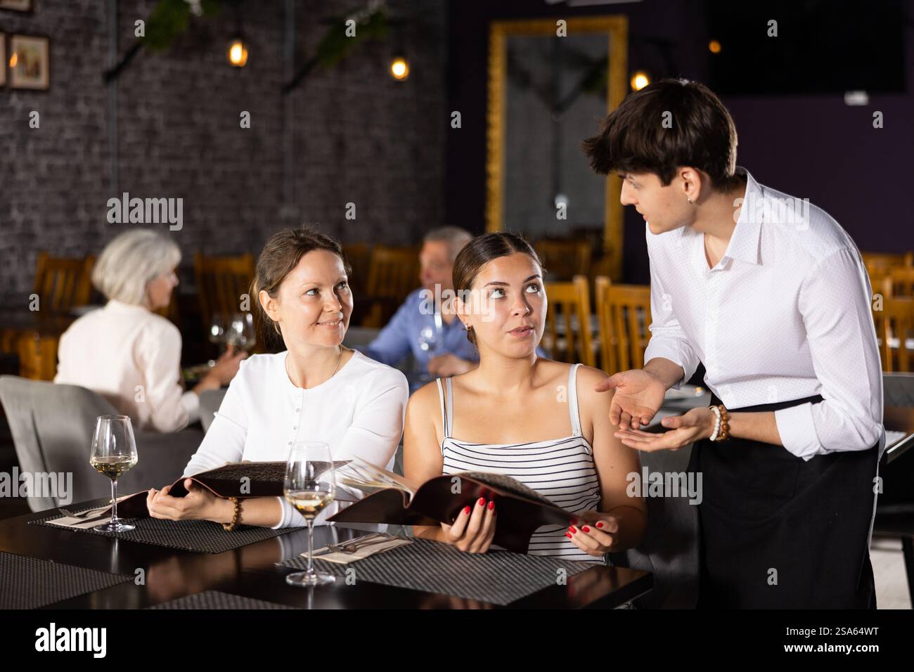 Female guests discussing menu with waiter at table in restaurant Stock ...