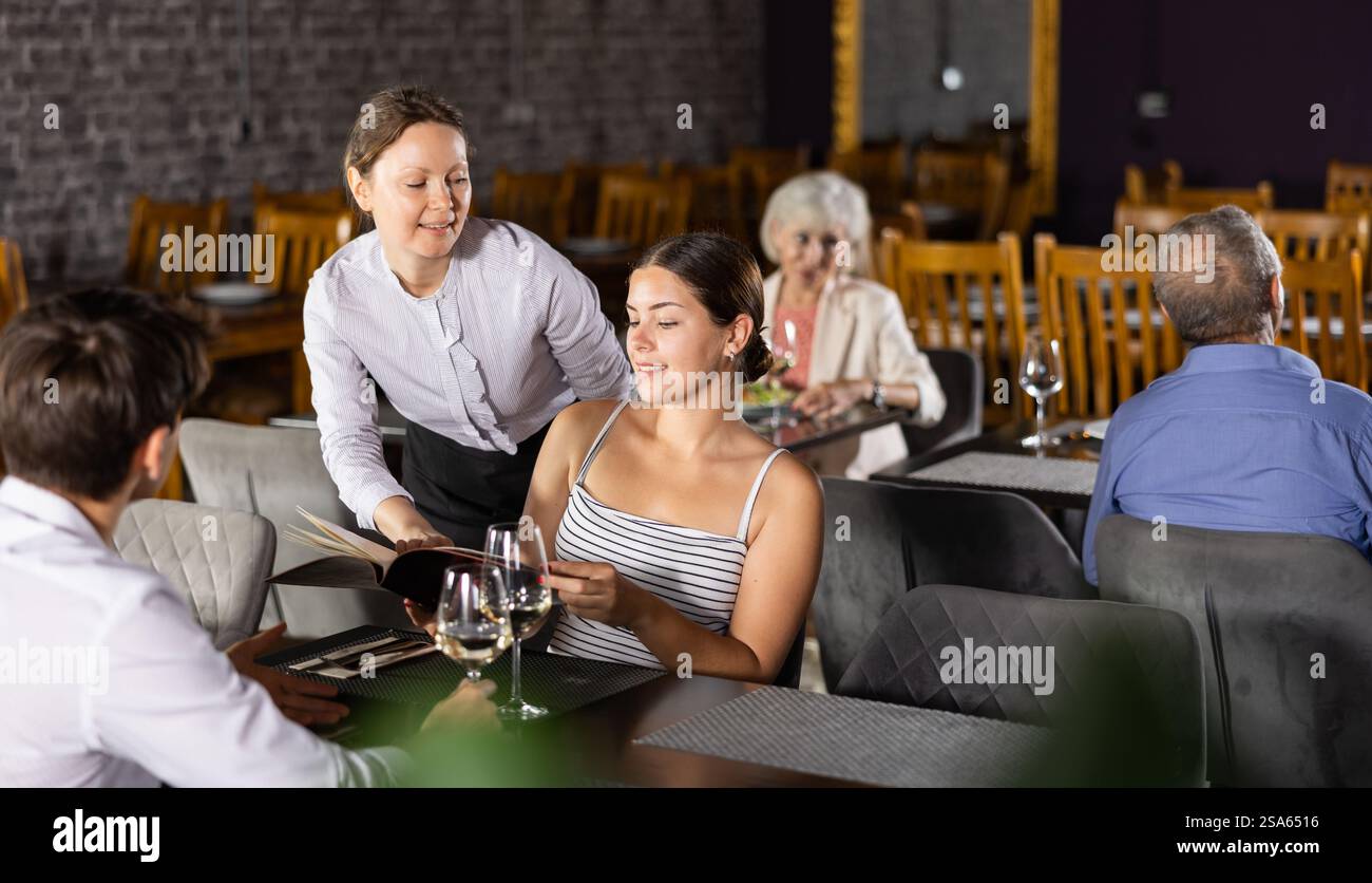 Female owner of restaurant offering dishes from menu to young couple ...
