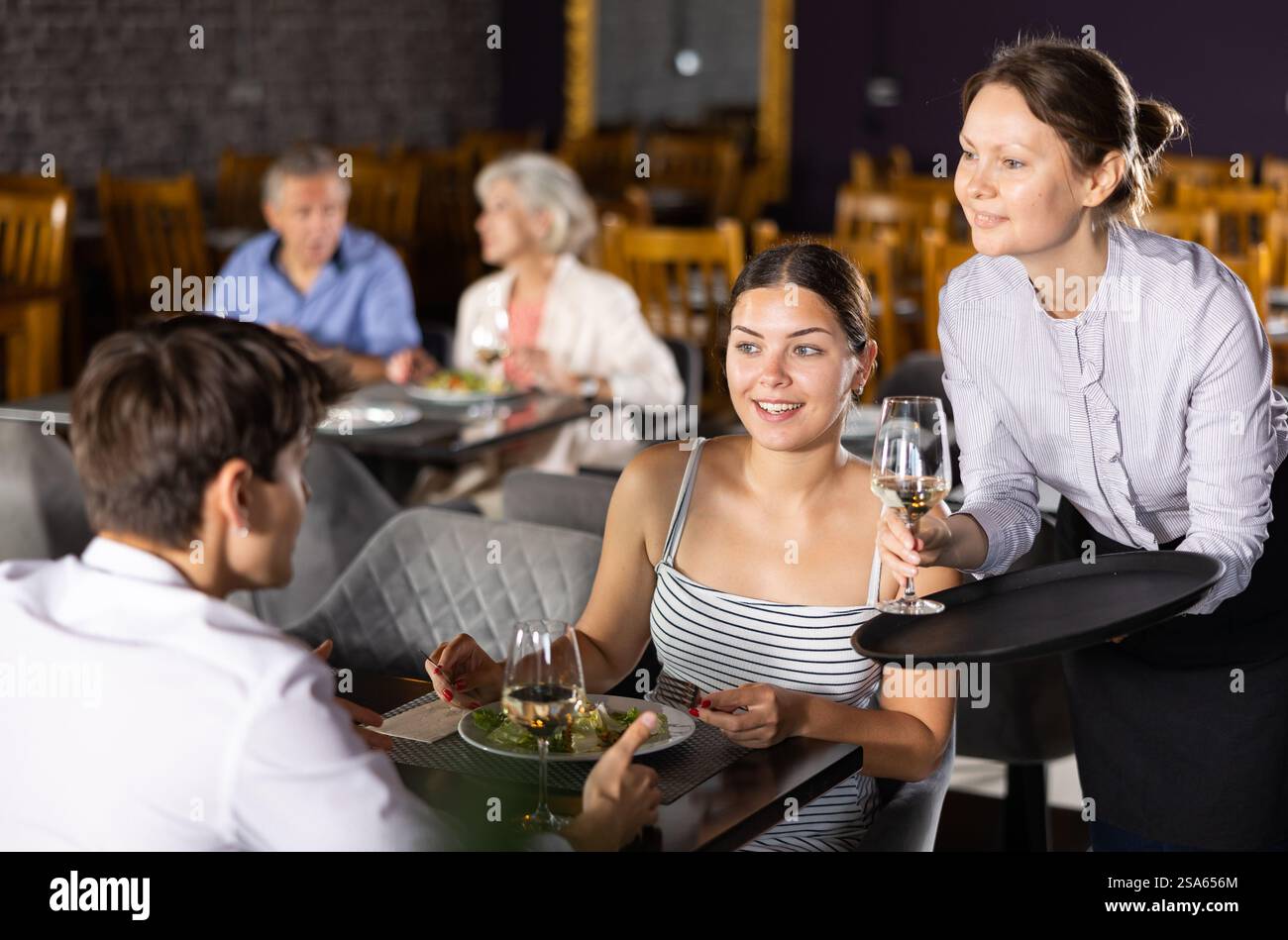 Waitress serves order of wine and wishes visitors young couple pleasant ...