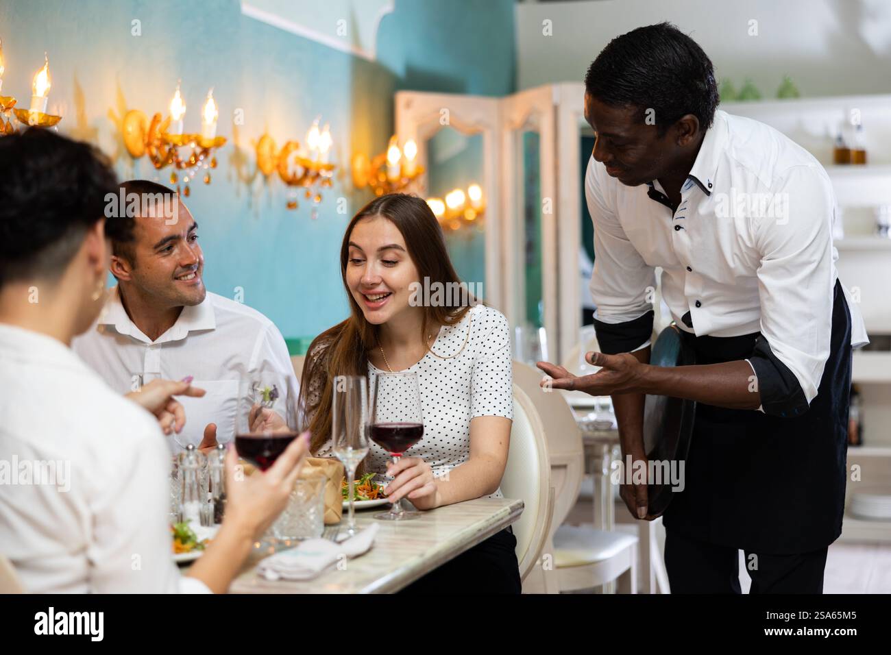 Positive couple talking with polite african american waiter while ...