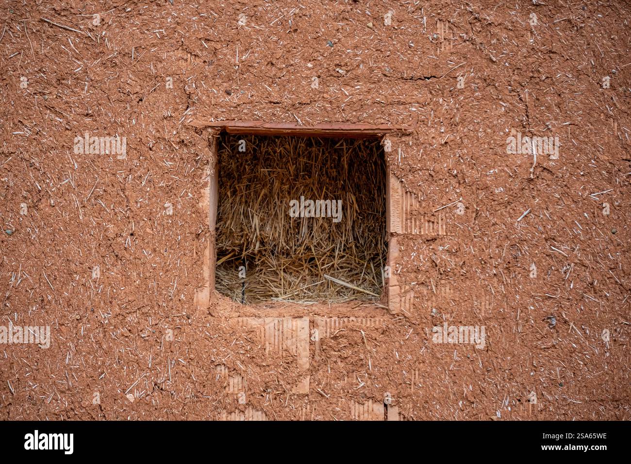 A window in a wall with straw in it. The window is small and the straw ...