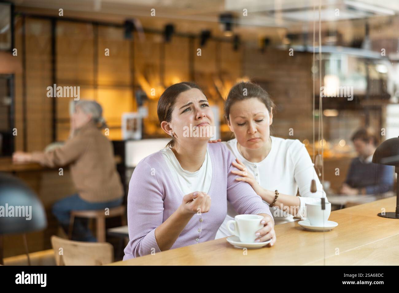 Portrait of two women comforting each other while sitting with cups of ...
