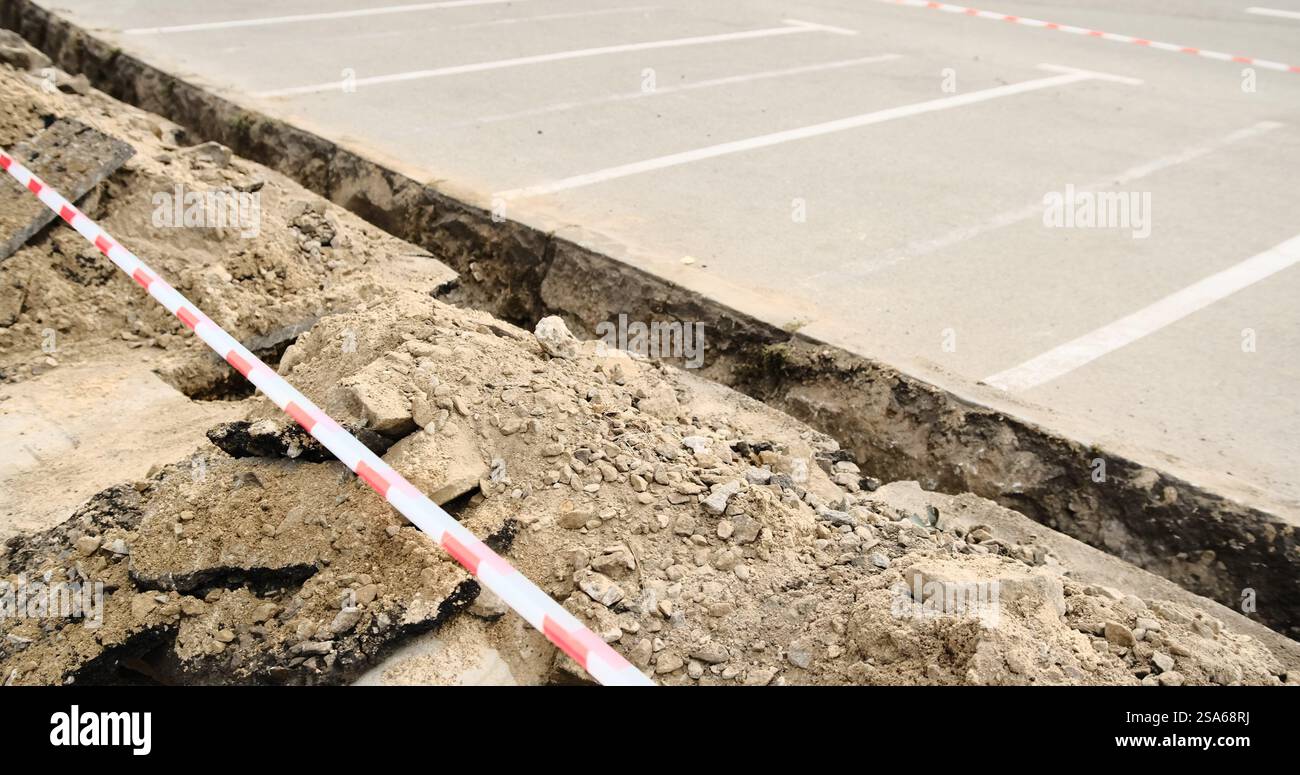 A freshly dug trench along a parking lot, marked with red and white ...