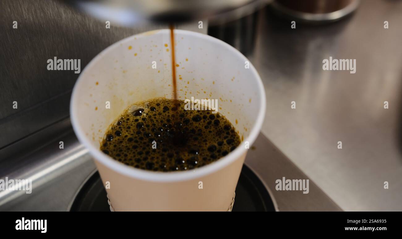 A close-up shot of freshly brewed coffee pouring into a paper cup from ...