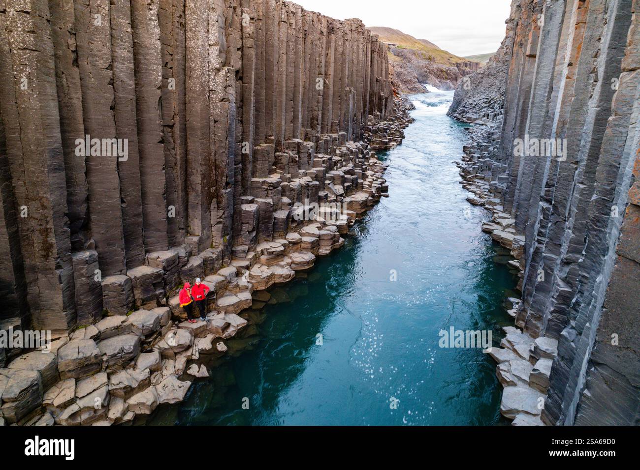 Aerial view of couple sitting in basalt Studlagil Canyon with river and unique columnar basalt ...
