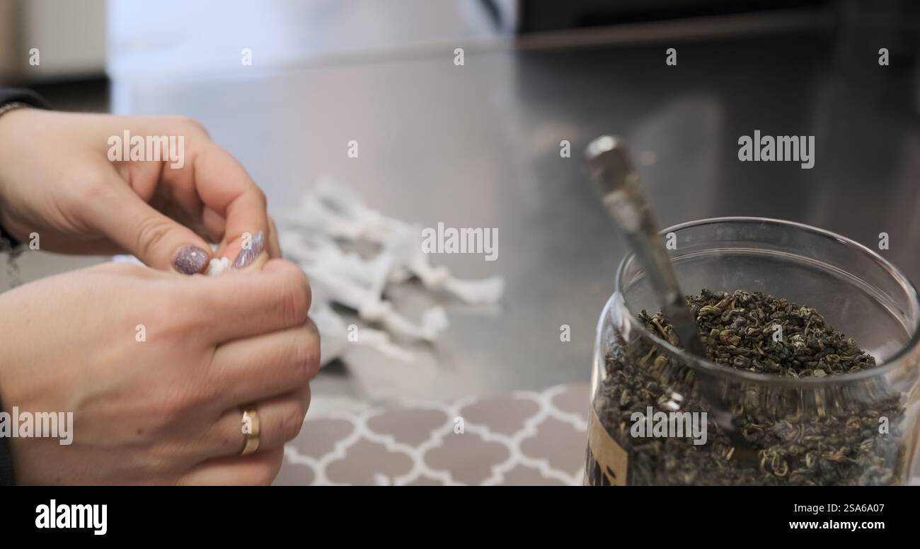 Female hands carefully portion loose tea into individual tea bags for ...