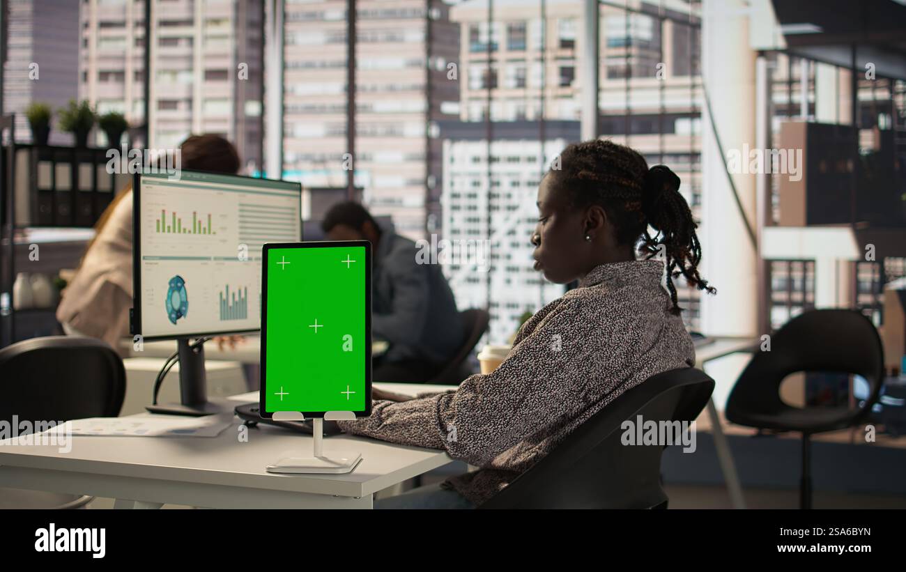Female manager seated at workstation with green screen on devices ...