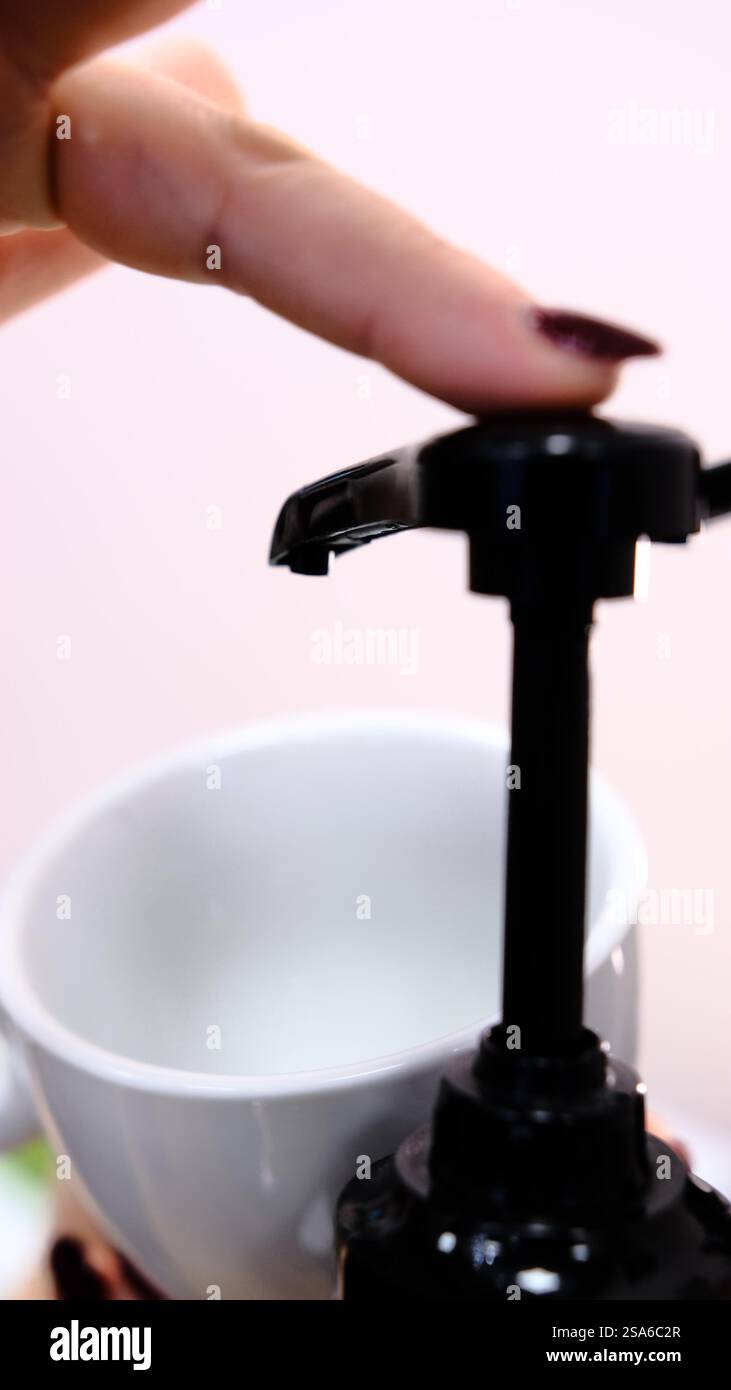 Barista adds red cherry syrup to a white coffee cup using a dispenser ...