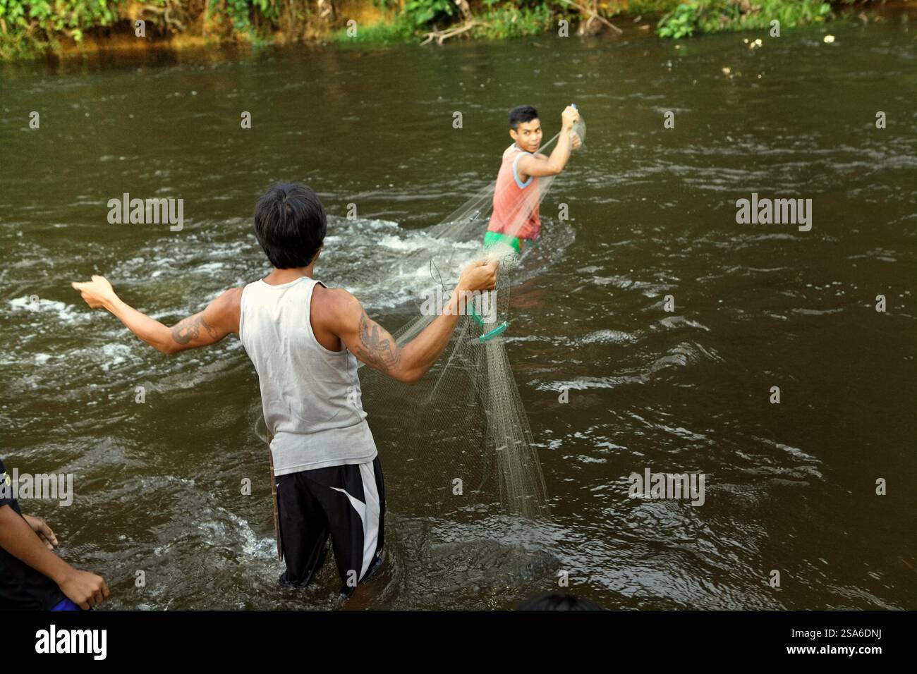 Men using a fishing net on a river near the longhouse of traditional ...