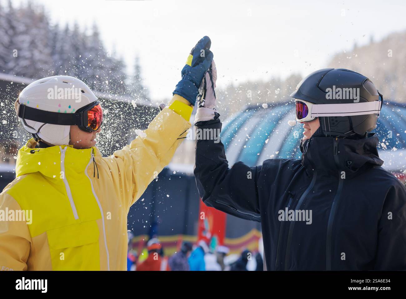 Two skiers in colorful ski gear smiling and slapping each other on the ...