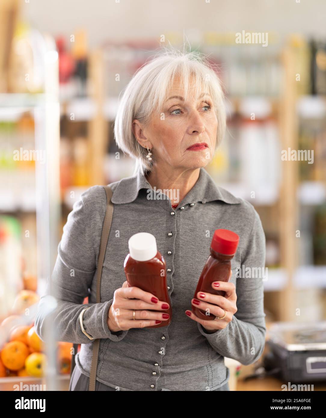 Elderly woman choosing ketchup in grocery store Stock Photo - Alamy