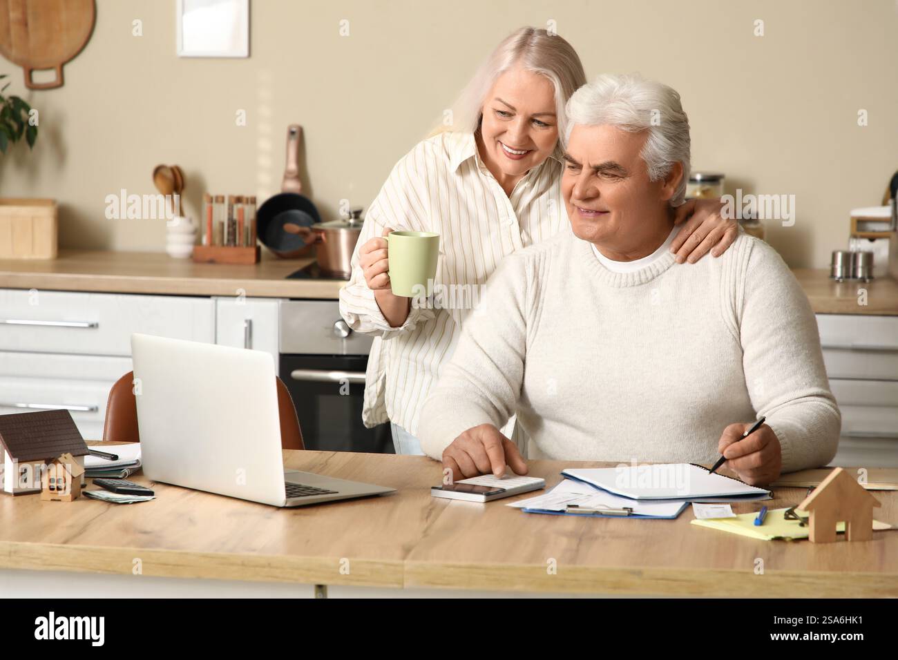 Senior couple with laptop calculating utility bills at table in kitchen ...