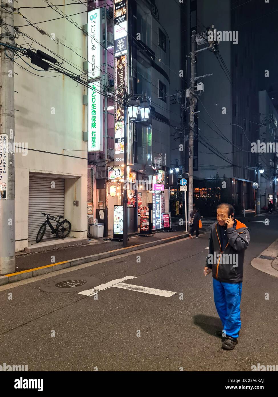 A Tokyo street at night time in Akabane, Japan with a man using a ...