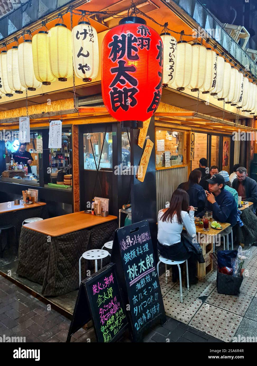 A restaurant at night with people and outdoor seating in the Akabane ...