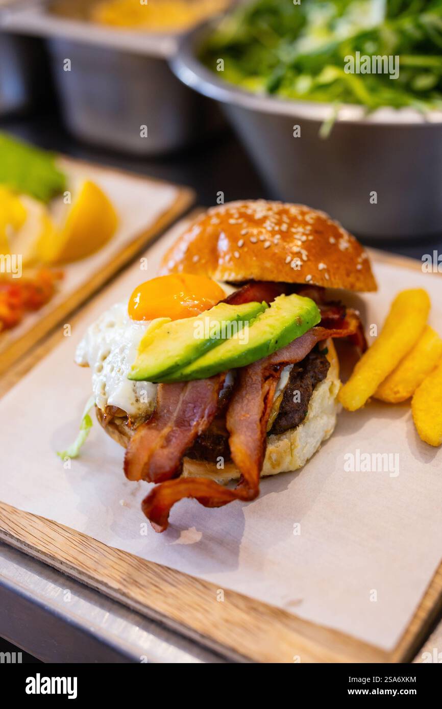 Beef burger on sesame bun topped with crispy bacon, sunny-side-up egg ...