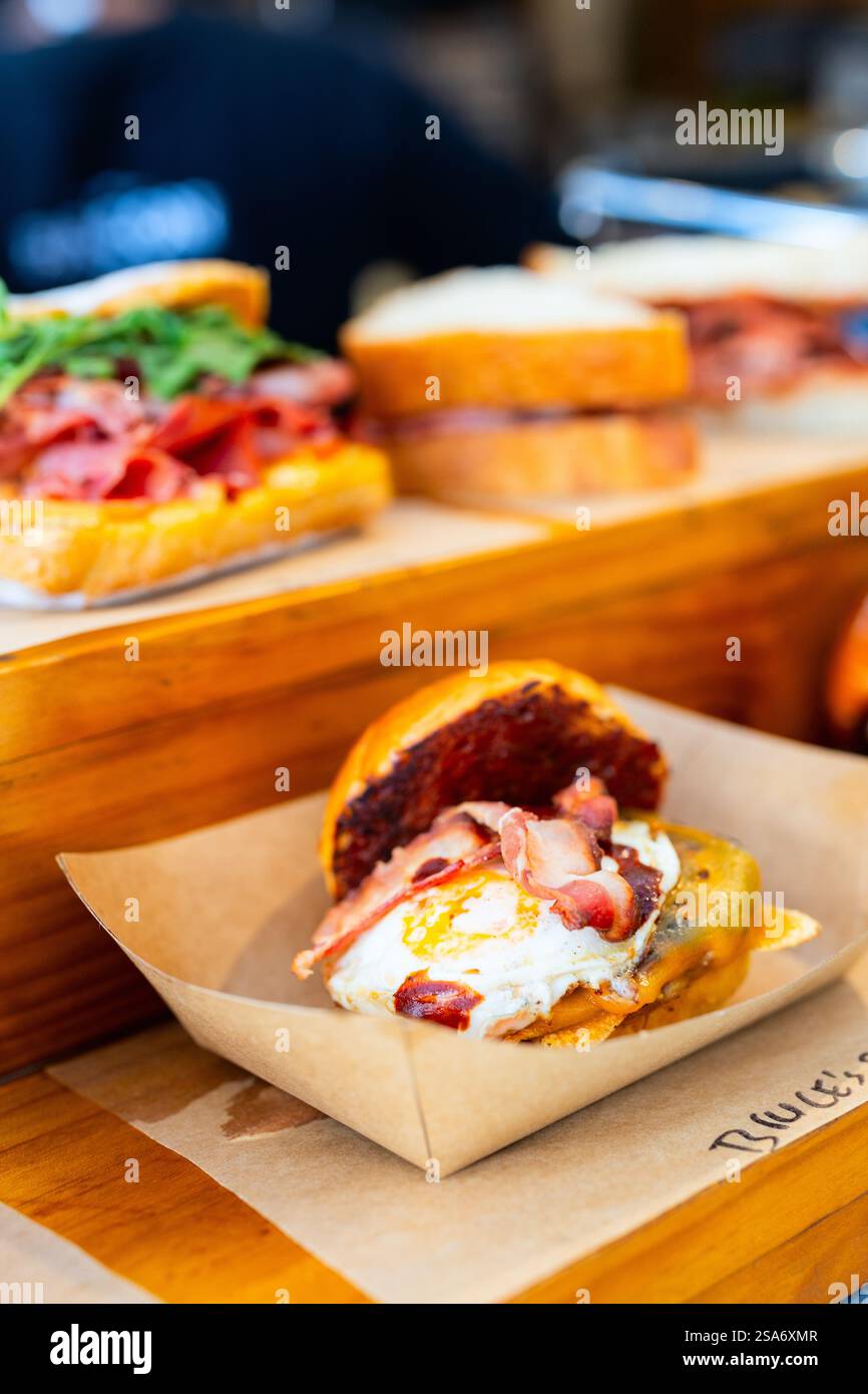 Mini burger on yellow bun topped with fried egg and crispy bacon strips ...