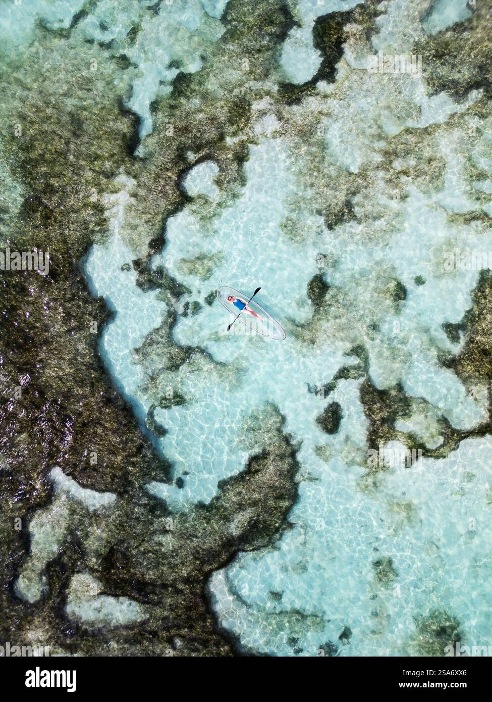 An aerial view of a woman kayaking in a transparent kayak over crystal ...