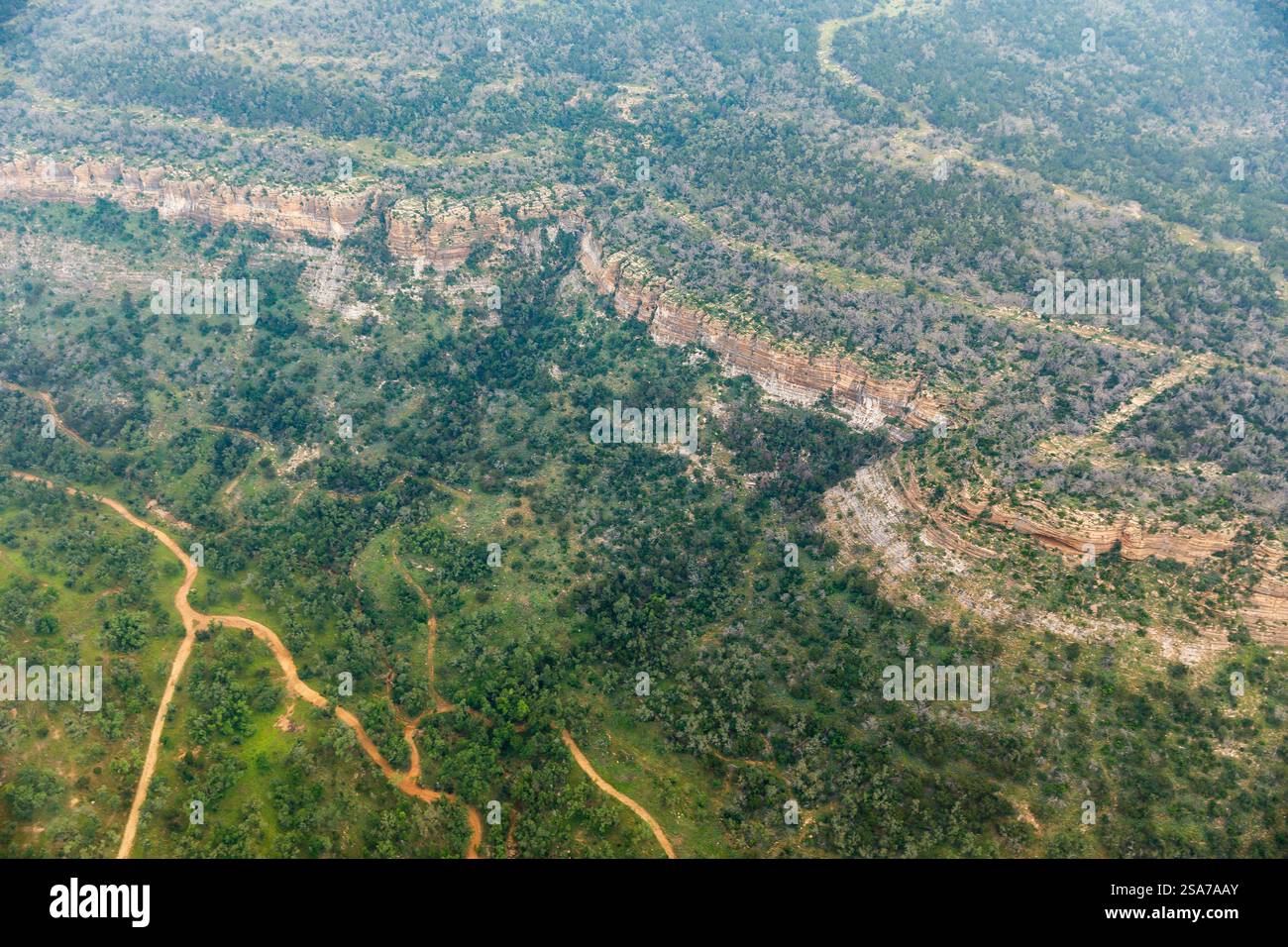 Aerial view of red rocky cliff ridge rising above green desert scrub ...