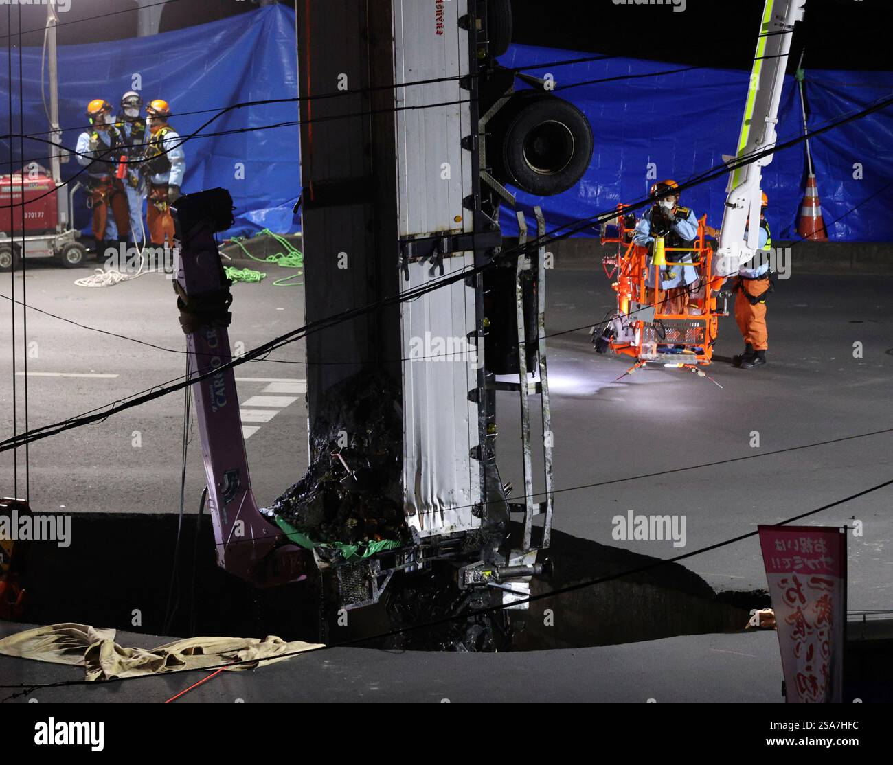 A fallen truck being pulled out of a road cave-in in Yashio City ...