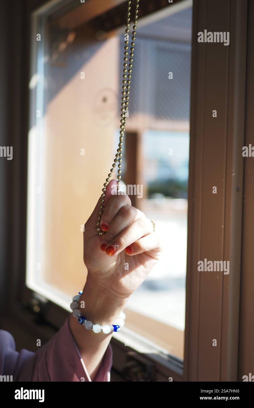 Hand pulling window blinds to let in natural light Stock Photo - Alamy