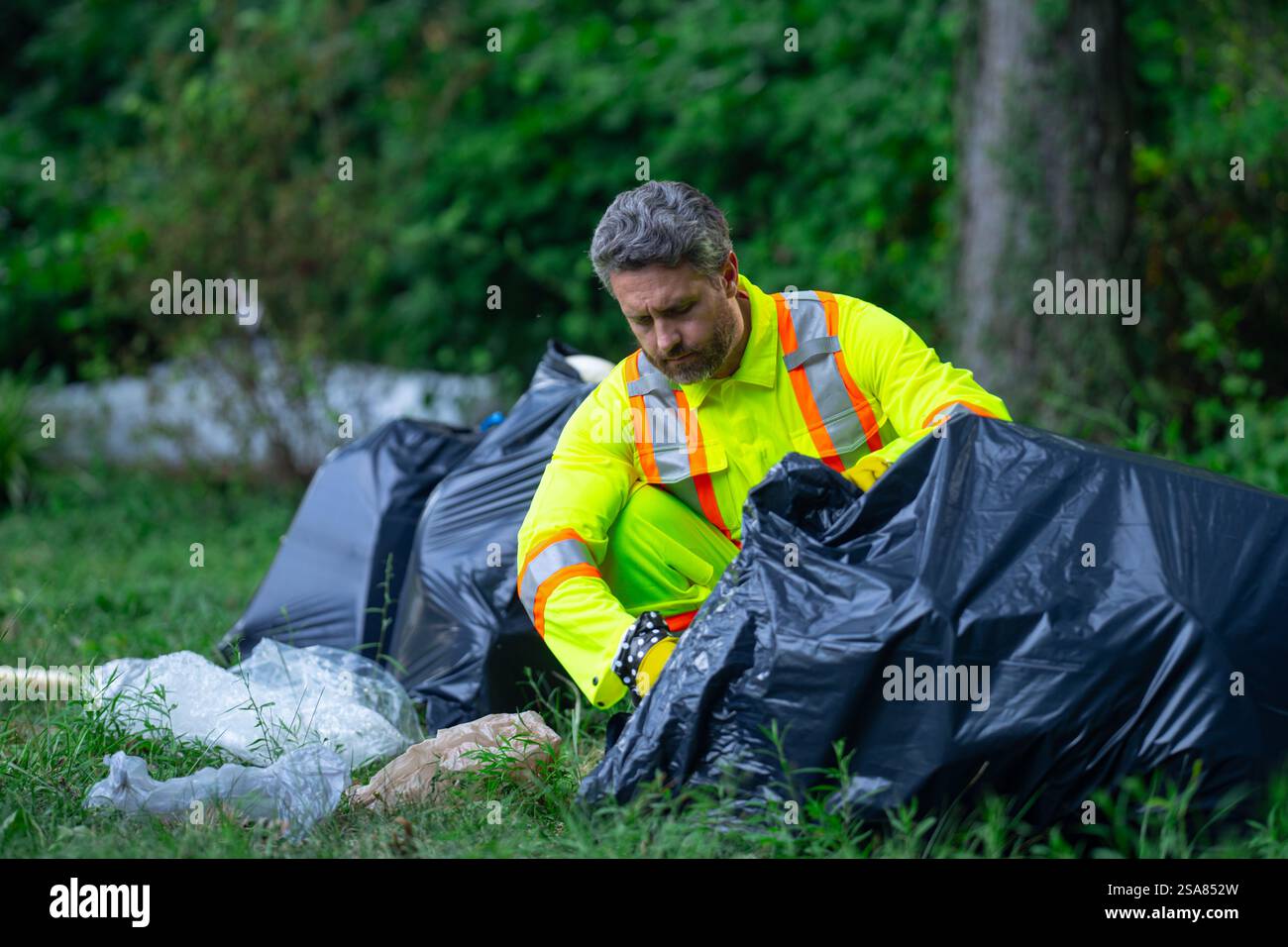 Volunteer in rubber gloves with trash bag clean up garbage on forest outdoor. Eco, environment ...
