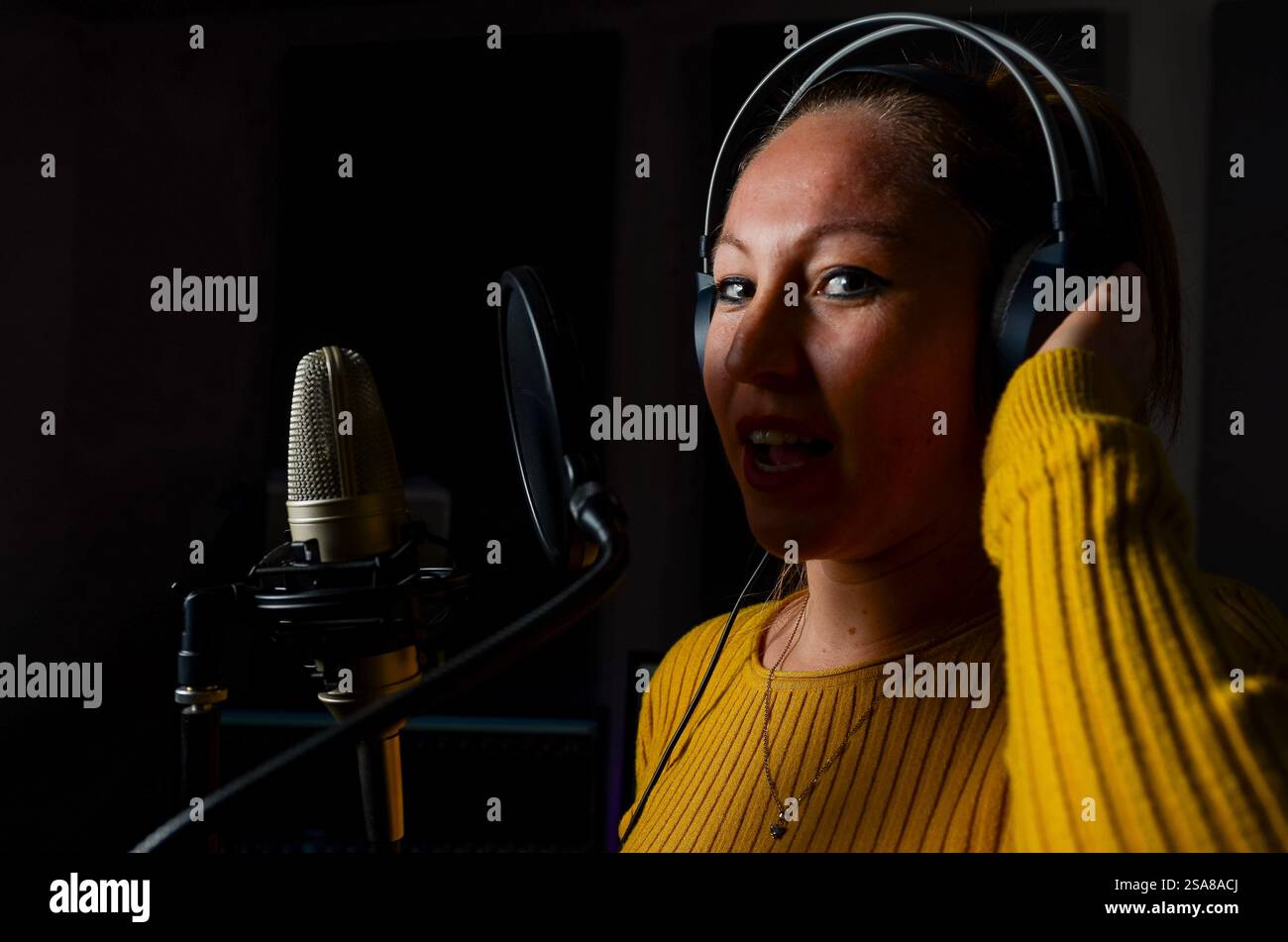 Female vocalist recording music track in dark professional studio using ...
