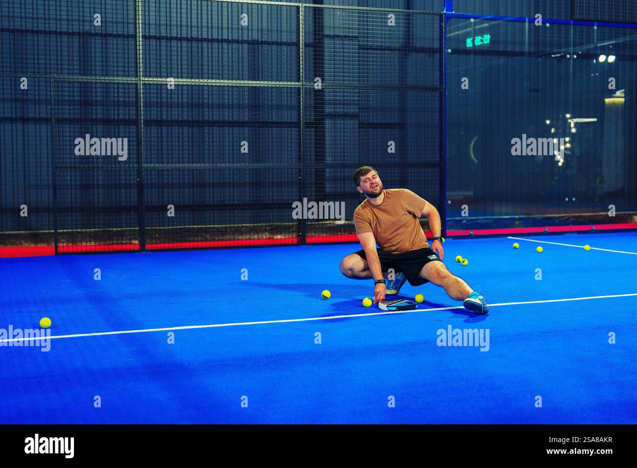 Man playing padel tennis and diving for a ball on a vibrant blue court ...